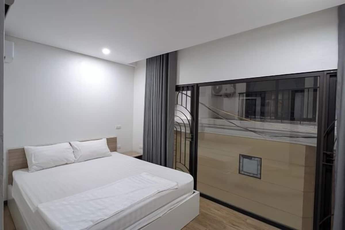Quarto de hotel moderno com cama, janela com vista para a rua e uma pequena janela na parede.