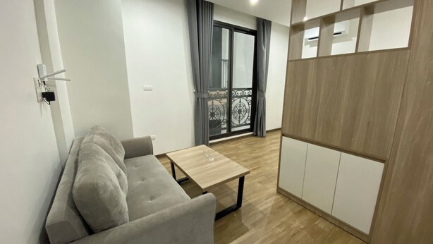 Uma sala de estar moderna com um sofá cinzento, uma mesa de centro de madeira e uma porta de vidro deslizante que dá para uma varanda.