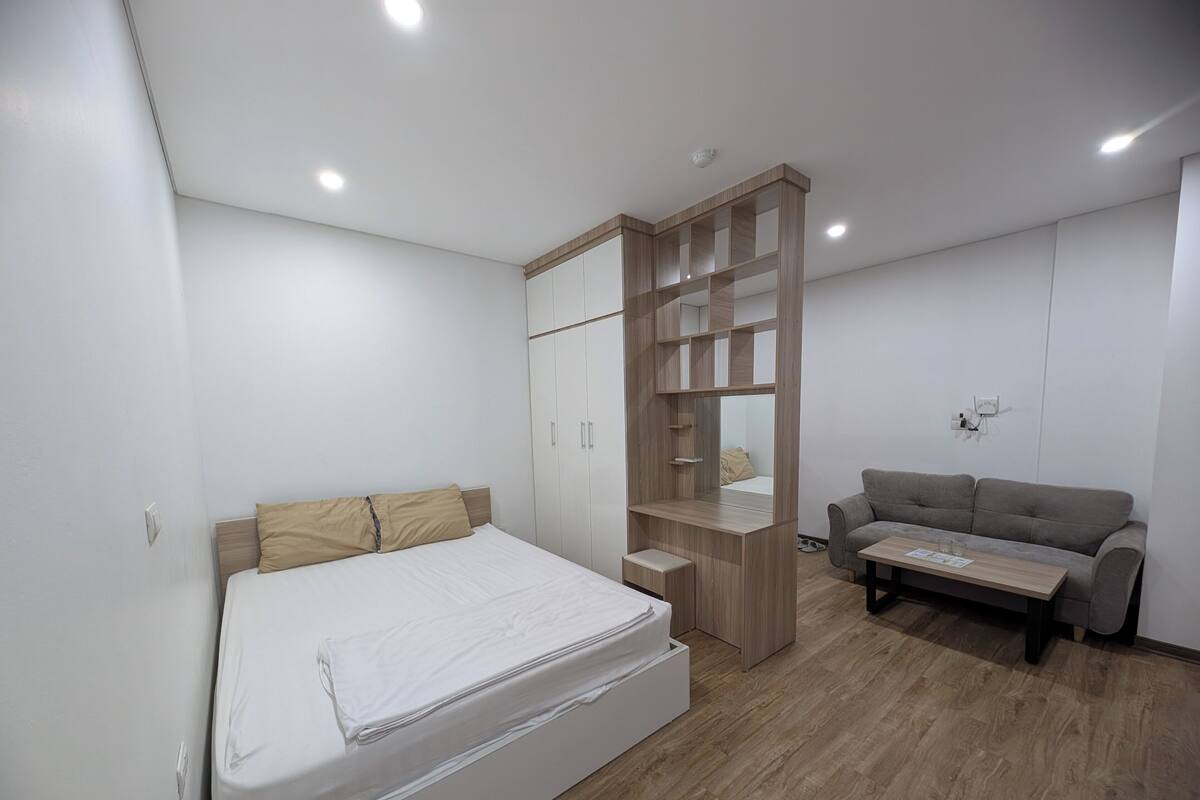 Quarto com uma cama, um guarda-roupa de madeira, um sofá cinzento e uma mesinha.