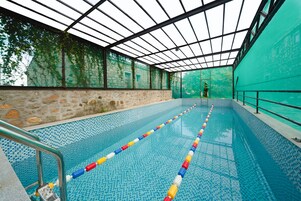 Piscina interior com divisórias de pistas bem definidas, paredes de pedra e teto de vidro.