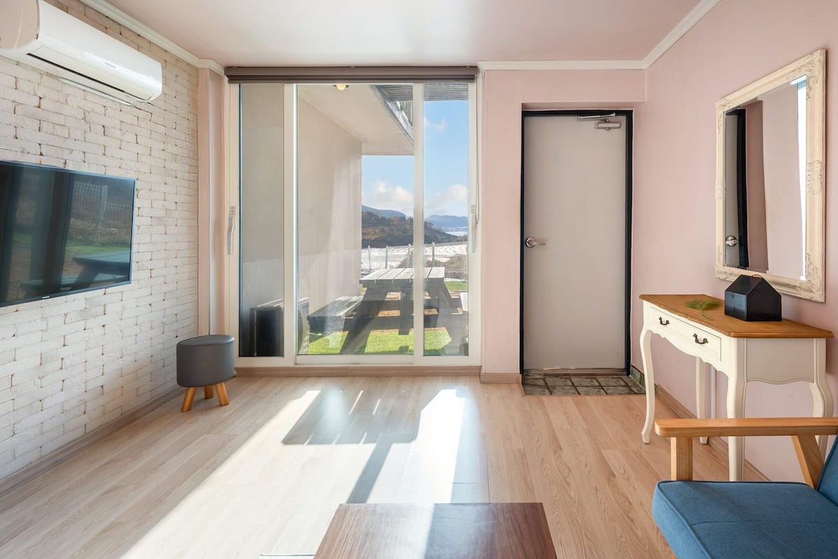 Uma sala de estar moderna com televisão, um sofá azul, um console de madeira e uma porta de vidro deslizante que dá para uma área externa com mesa de piquenique.