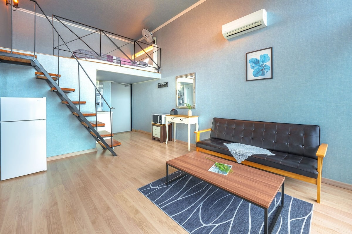Um espaço compacto com cozinha compacta, sofá, mesa de centro, escada e pequena escrivaninha.