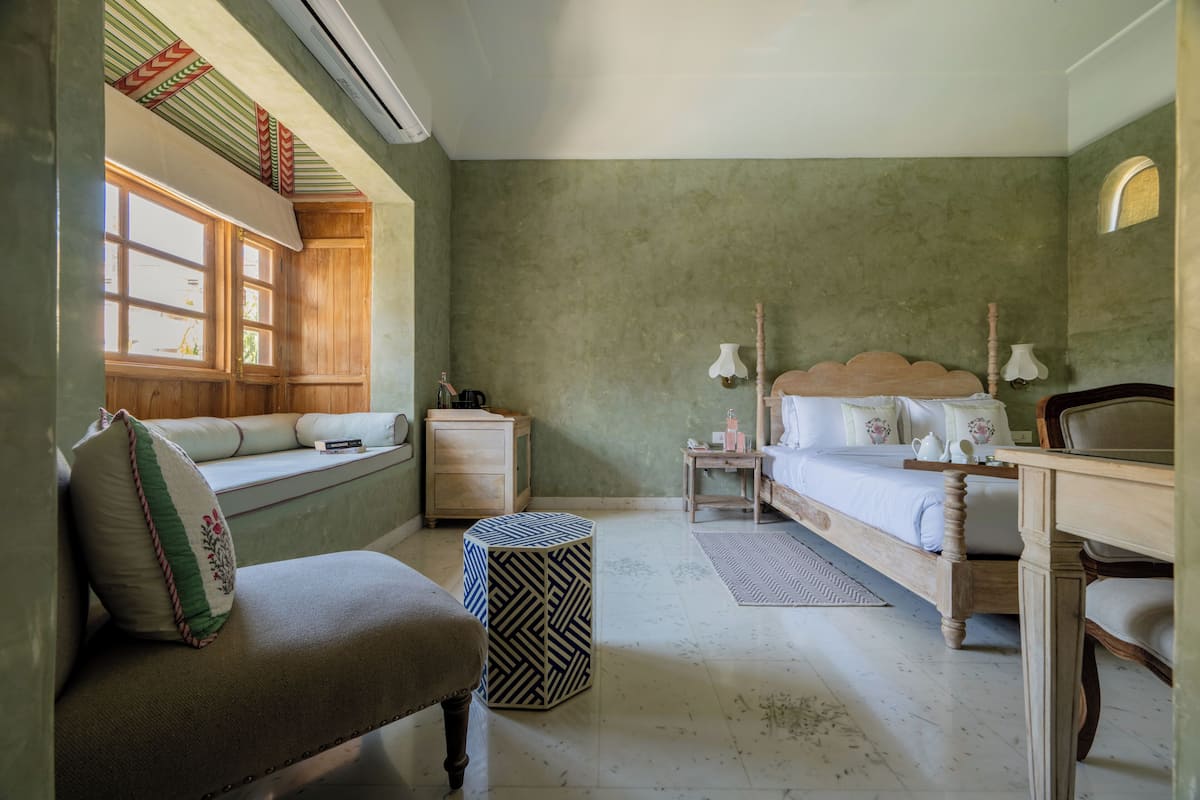Quarto com cama, mesa de cabeceira, cadeira e janela com vista.