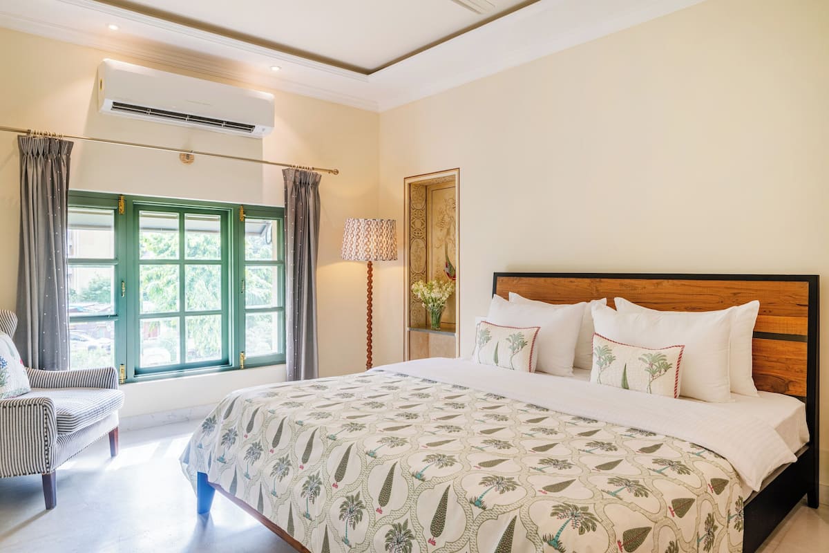 Quarto com cama, cadeira, janela com cortinas, ar-condicionado e luminária.