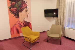 Quarto com duas cadeiras, uma TV na parede e um pôster grande.