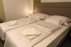 Uma cama de casal com lençóis e almofadas brancos, um abajur e uma parede com padrão floral.