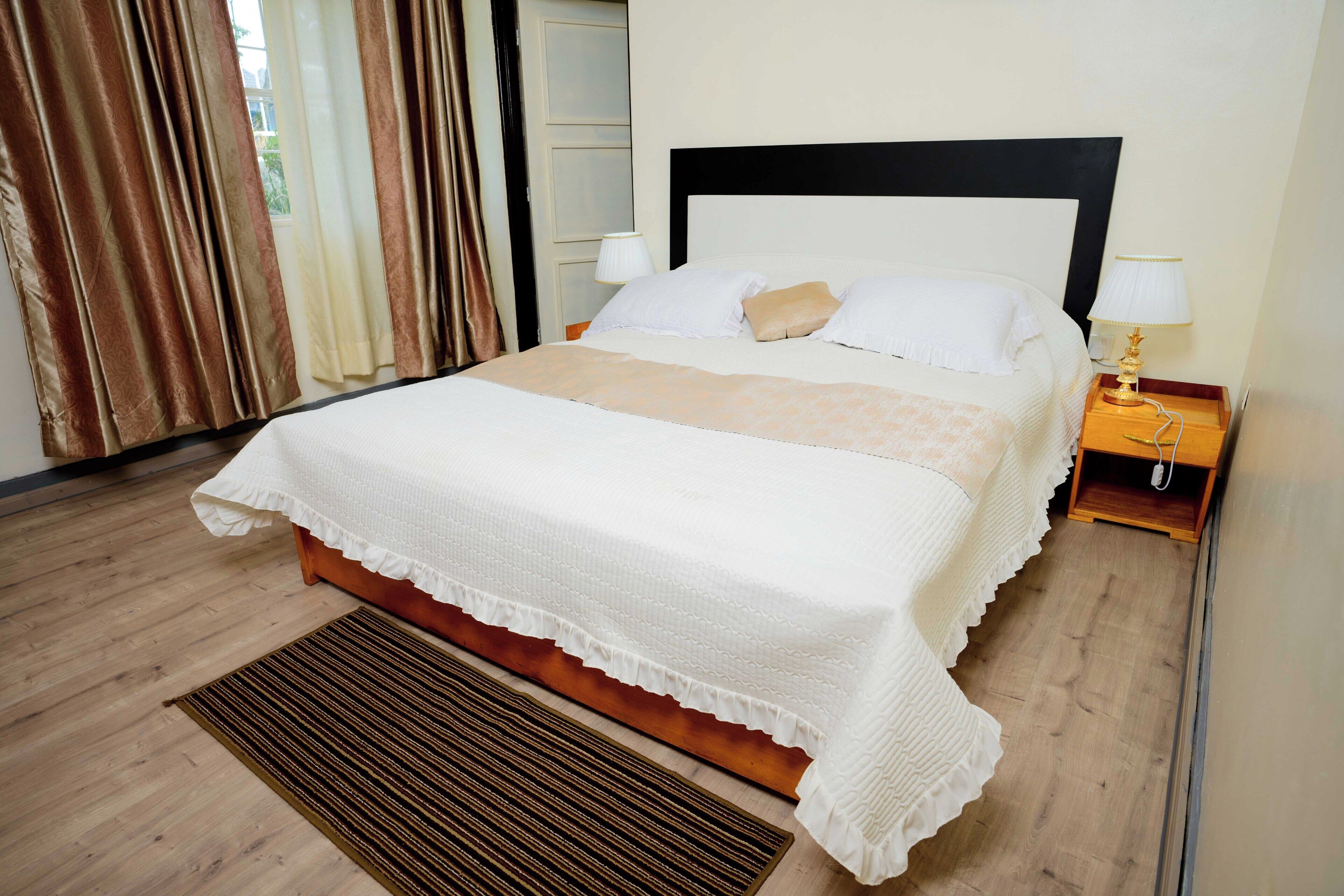Uma cama bem arrumada com um edredom branco e bege, uma cabeceira de madeira e duas luminárias de mesa em um criado-mudo.