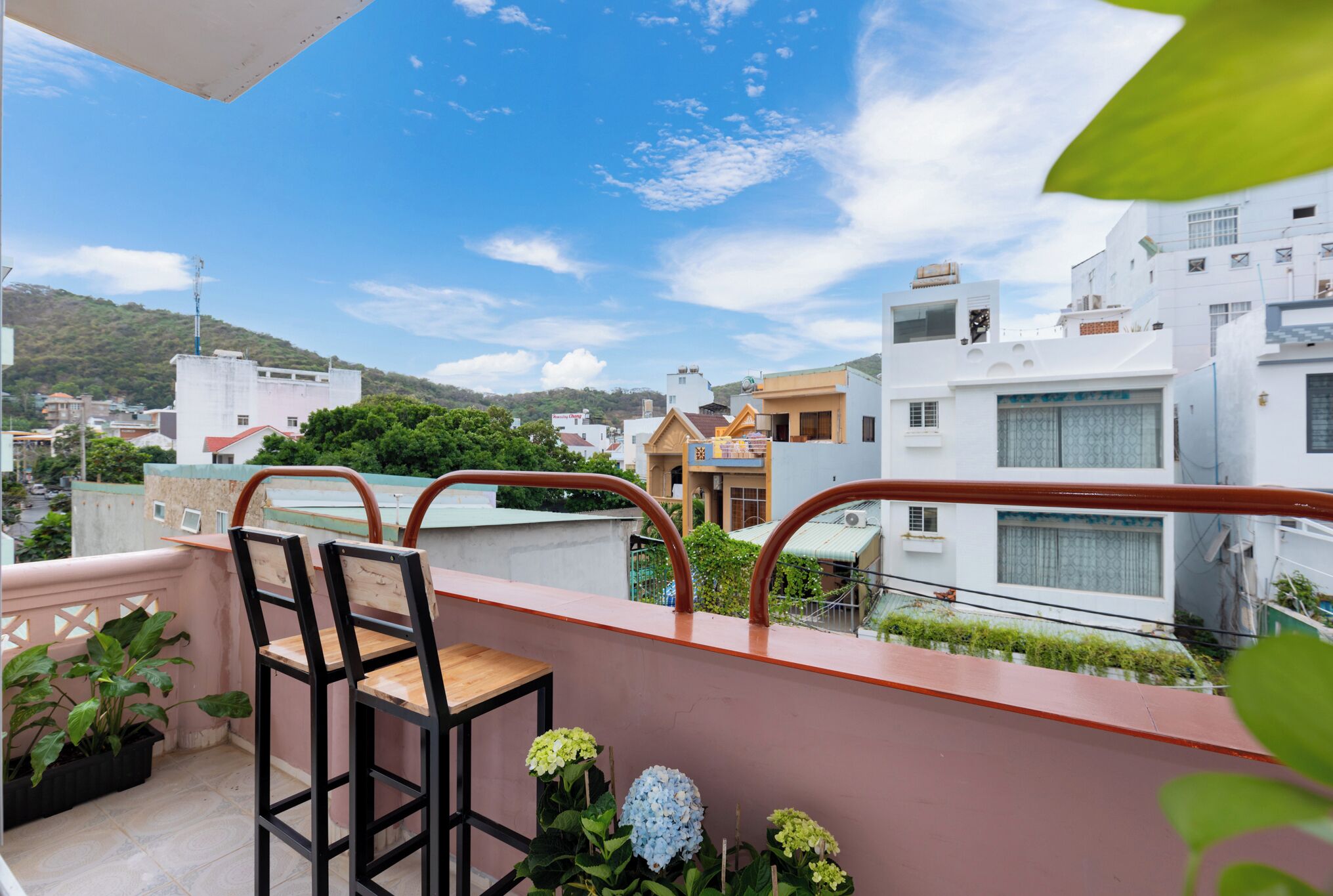 Varanda com mesa e cadeiras de madeira, com vista para área residencial com edifícios brancos e vegetação.