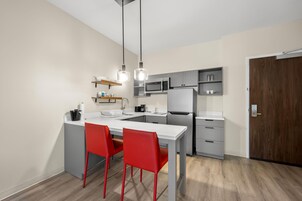 Cozinha moderna com ilha central, duas cadeiras vermelhas, micro-ondas e frigorífico.