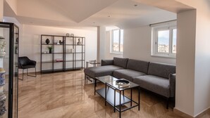 Uma sala de estar moderna com um sofá seccional cinza, uma mesa de centro de vidro, uma estante de metal preta e uma cadeira preta.