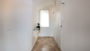 Um corredor com chão de mármore, uma pequena planta em uma prateleira de vidro e uma porta com interruptor de luz.