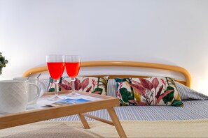 Uma cama com cabeceira de madeira, almofada florida e bandeja com dois copos de líquido vermelho, uma caneca e uma colher.