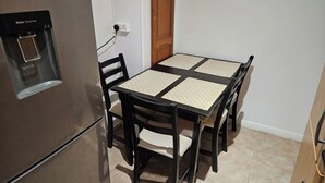 Uma cozinha compacta com um dispensador de água, uma mesa de jantar com quatro cadeiras e uma porta de madeira.