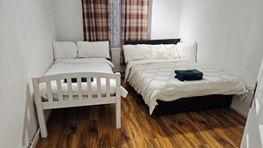 Quarto pequeno e limpo, com duas camas, soalho de madeira e cortinas xadrez.