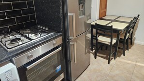 Uma cozinha com fogão preto, geladeira e mesa de jantar com cadeiras.