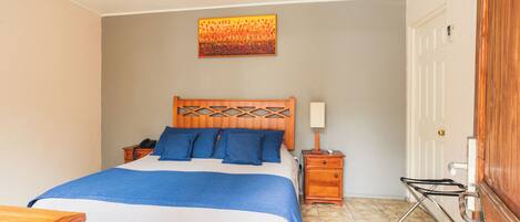 Quarto de hotel com cama, mesas de cabeceira, um criado-mudo, uma obra de arte na parede e uma porta.