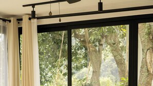 Quarto com uma cama grande, cabeceira de madeira e vista para um jardim exuberante através de uma porta de vidro deslizante.