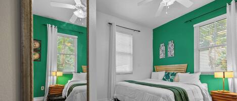 Quarto com duas camas, paredes verdes, roupa de cama branca e um tapete colorido.