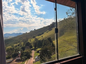 Visão através de uma janela de uma paisagem montanhosa com campos em socalcos e céu claro.