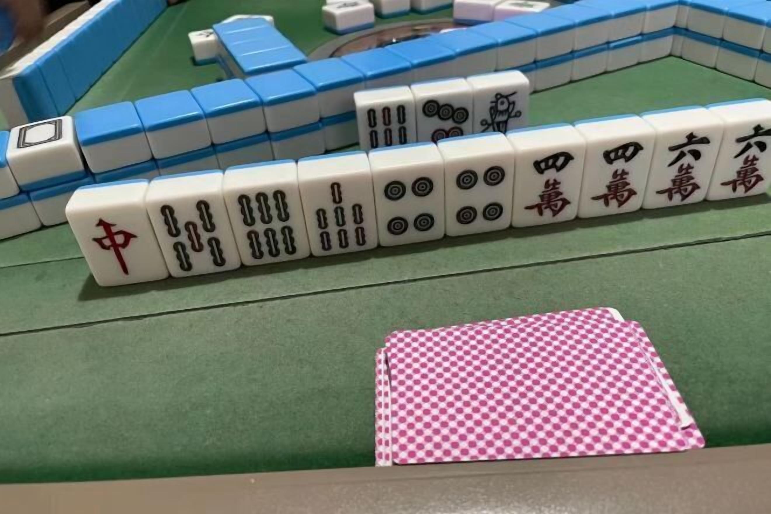 Conjunto de peças de Mahjong dispostas sobre uma mesa verde com um tecido xadrez rosa.