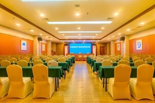 Uma sala de conferências com mesas e cadeiras dispostas em fileiras, um palco com uma tela e um púlpito.