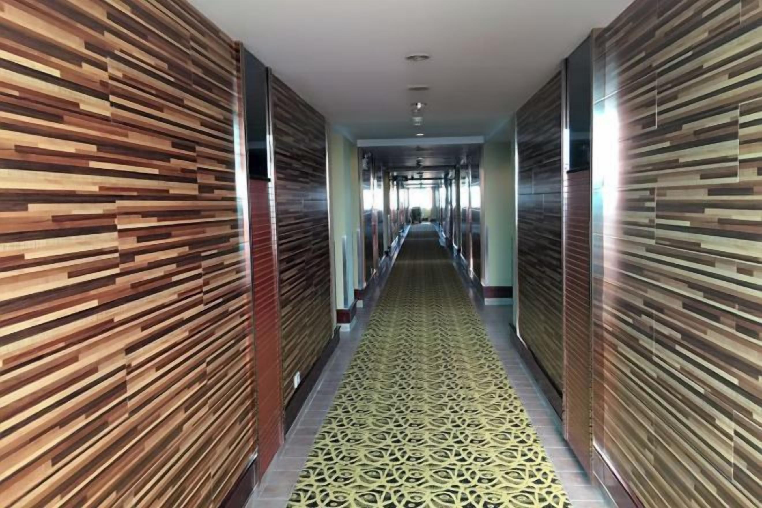 Um corredor com paredes e carpete estampados, que leva a uma área iluminada no final.