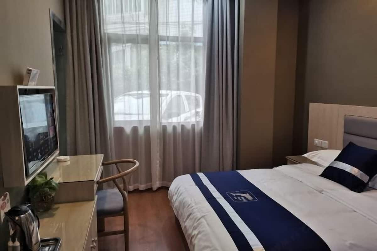 Quarto de hotel com cama, escrivaninha, cadeira, televisão e janela com cortinas.