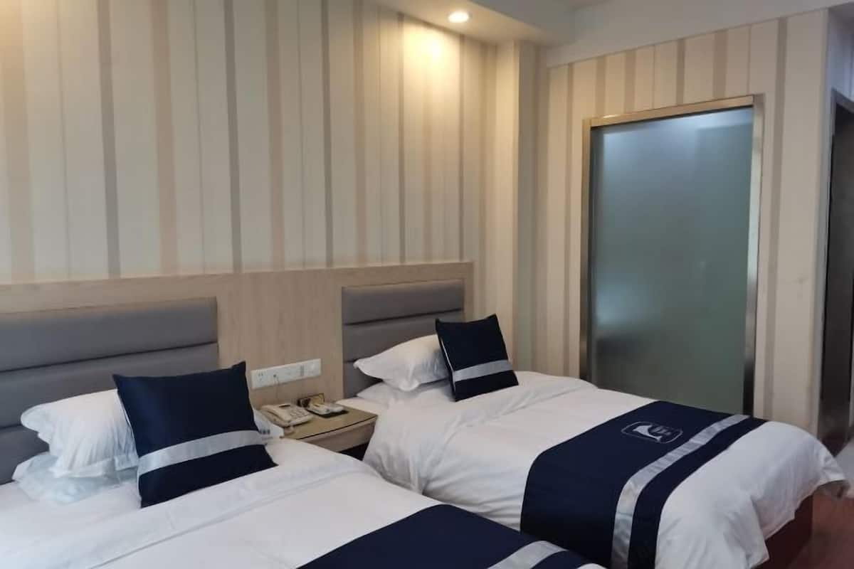 Quarto de hotel com duas camas, uma mesa de cabeceira com telefone e uma porta com painel de vidro jateado.