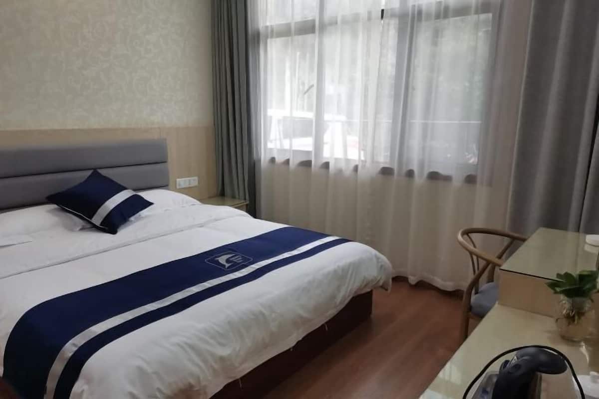 Quarto de hotel com cama, escrivaninha, cadeira e janela com cortinas.