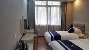 Quarto de hotel com duas camas, uma secretária com cadeira, um espelho e uma janela com cortinas.