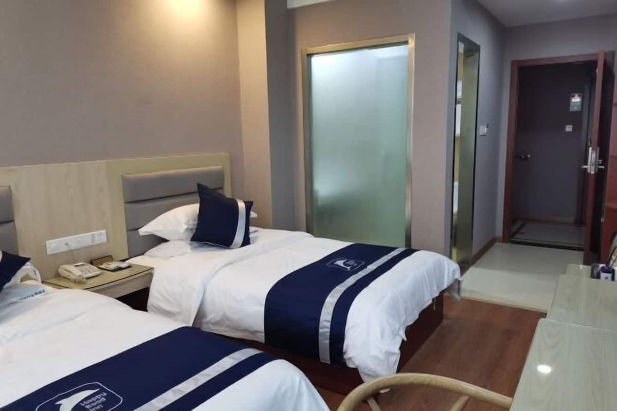 Quarto de hotel com duas camas, um painel de cabeceira em madeira, uma mesa de cabeceira com telefone e uma porta com painel de vidro fosco.