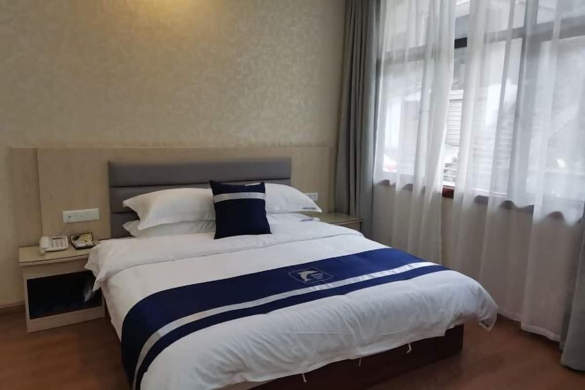 Quarto de hotel com cama, mesa de cabeceira com telefone e janela com cortinas.