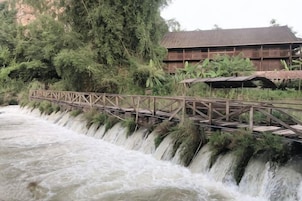 Uma ponte de madeira sobre um rio caudaloso, com um edifício ao fundo.