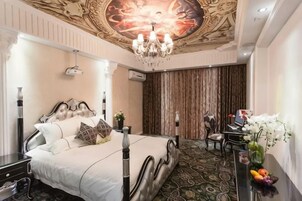 Quarto de hotel com uma cama grande, um candelabro, uma escrivaninha com um vaso de flores e um tapete estampado.