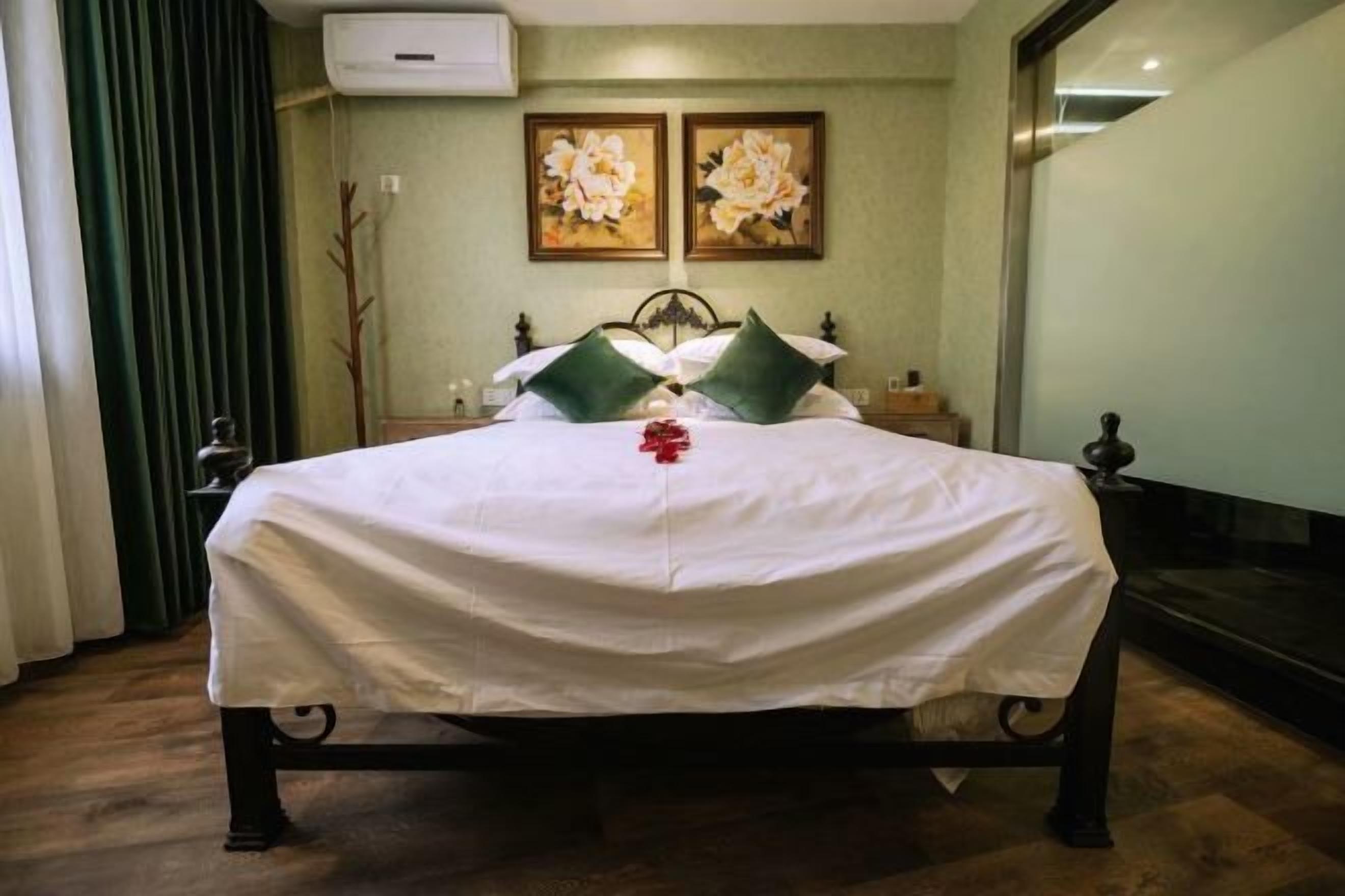 Uma cama bem arrumada com lençol branco e duas almofadas verdes, uma cabeceira de madeira e dois quadros florais emoldurados na parede.