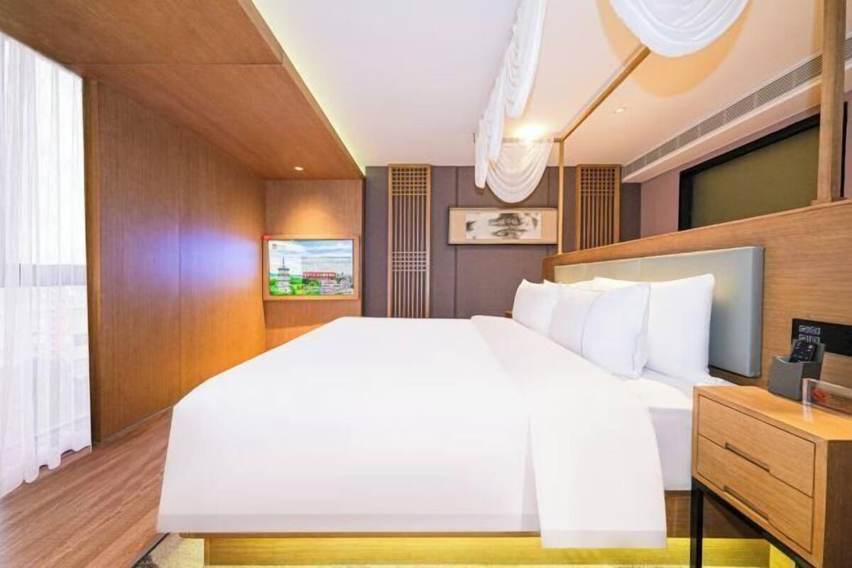 Quarto de hotel com cama grande, mesa de cabeceira e televisão na parede.