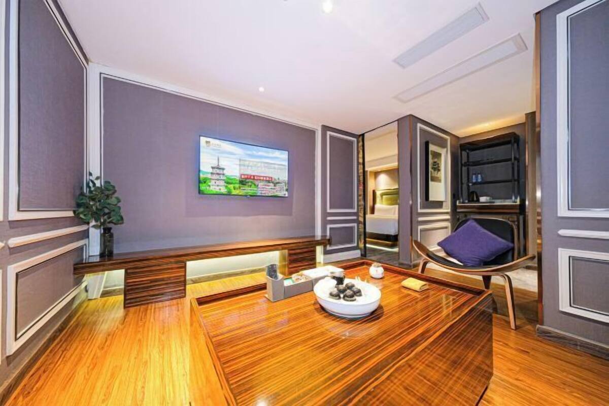 Um hall de hotel moderno com um balcão de recepção de madeira, uma televisão na parede e uma área de estar com uma cadeira e uma mesa pequena.