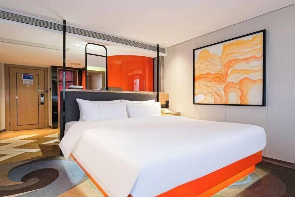 Quarto de hotel moderno com uma cama grande, um guarda-roupa, uma escrivaninha e uma pintura na parede.