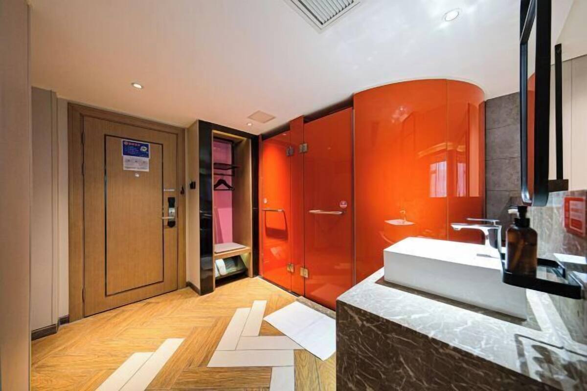 Um banheiro de hotel moderno com bancada de mármore, box de vidro e porta de madeira.