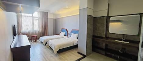 Quarto de hotel com escrivaninha, duas camas, televisão e banheiro com espelho.