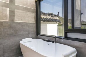 Uma casa de banho moderna com uma banheira independente, uma janela grande e vista para arquitetura tradicional.
