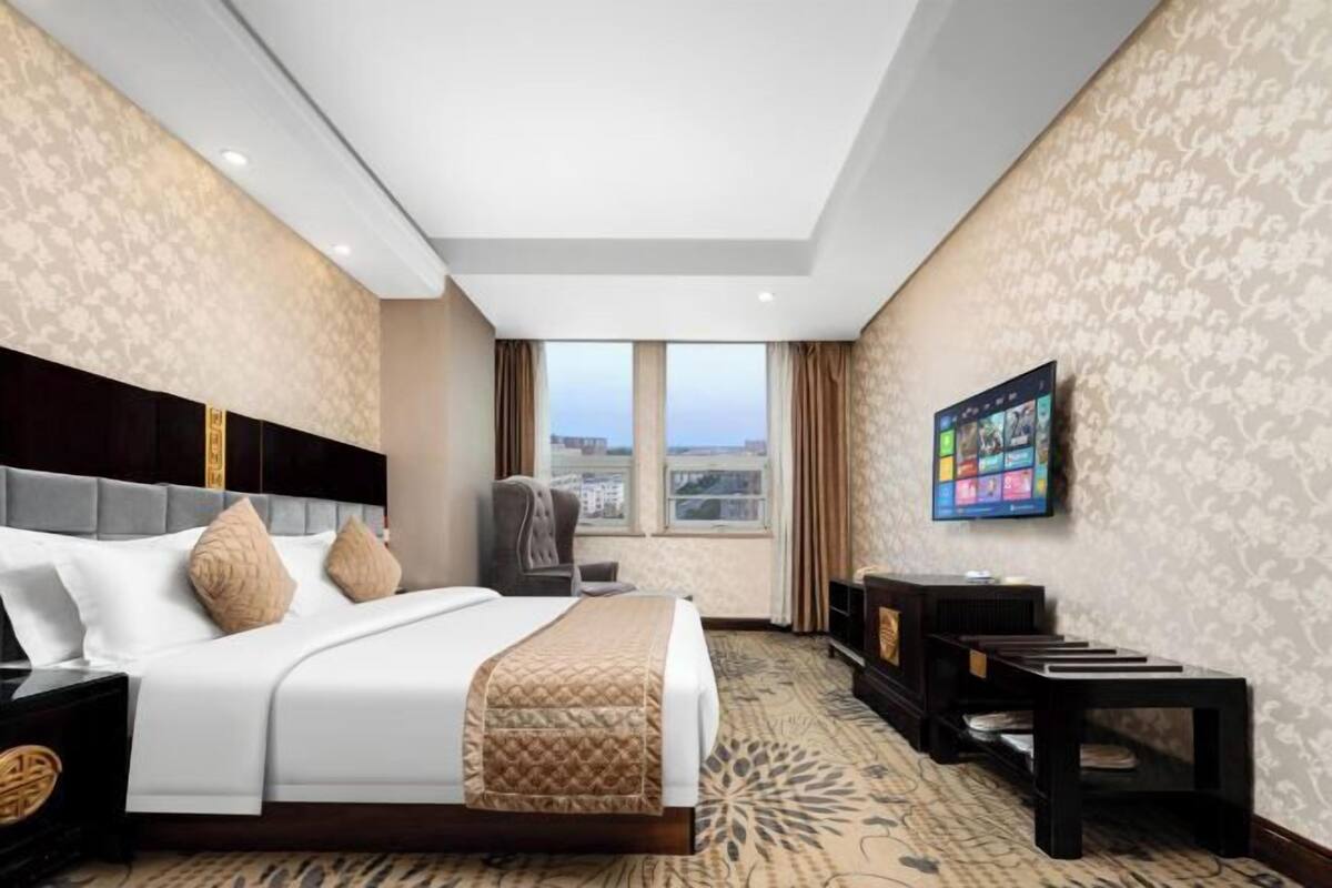 Quarto de hotel com uma cama, televisão, janela e vista para a cidade.