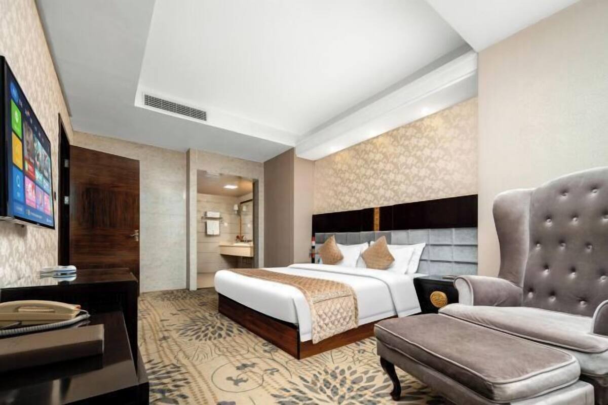 Quarto de hotel com cama, área de estar, mesa com telefone e TV na parede.