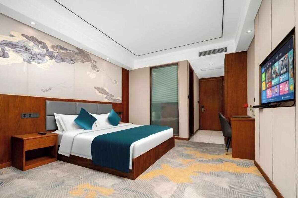 Quarto de hotel moderno com uma cama grande, uma escrivaninha, uma TV e um mural decorativo na parede.