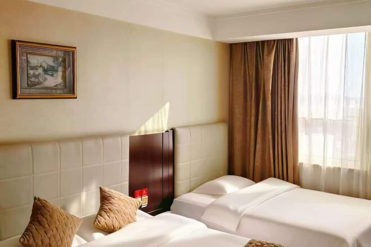 Quarto de hotel com duas camas, cabeceira, um quadro na parede e uma janela com cortinas.