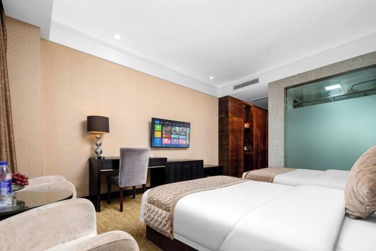 Quarto de hotel com cama, escrivaninha, cadeira, televisão e uma janela grande.