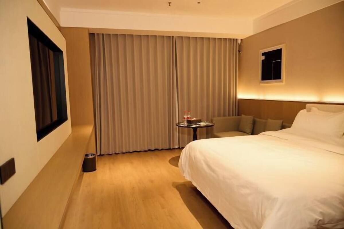 Quarto de hotel com cama, uma pequena mesa, um sofá, janela e cortinas.