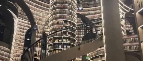 Uma biblioteca com vários níveis, estantes organizadas em espiral, uma escadaria central e design arquitetônico moderno.