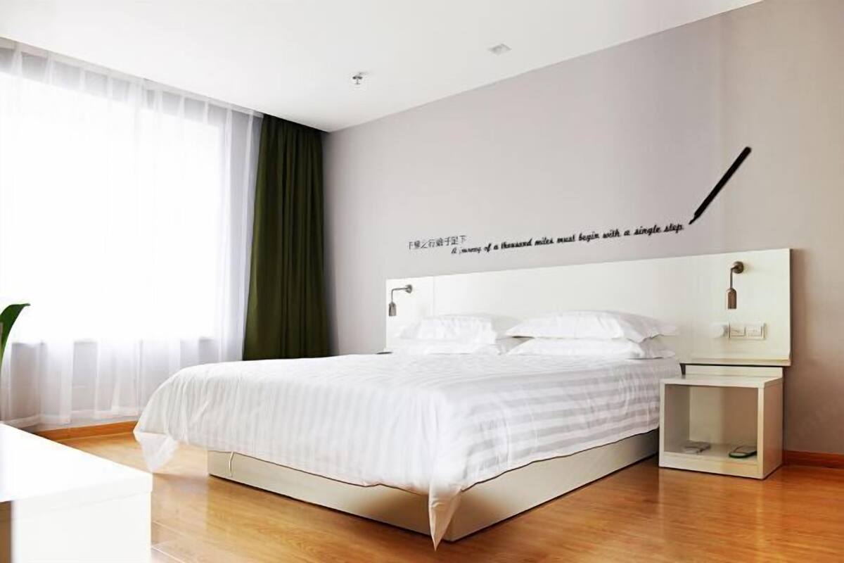 Quarto moderno com cama grande, mesa de cabeceira e luminária na parede.