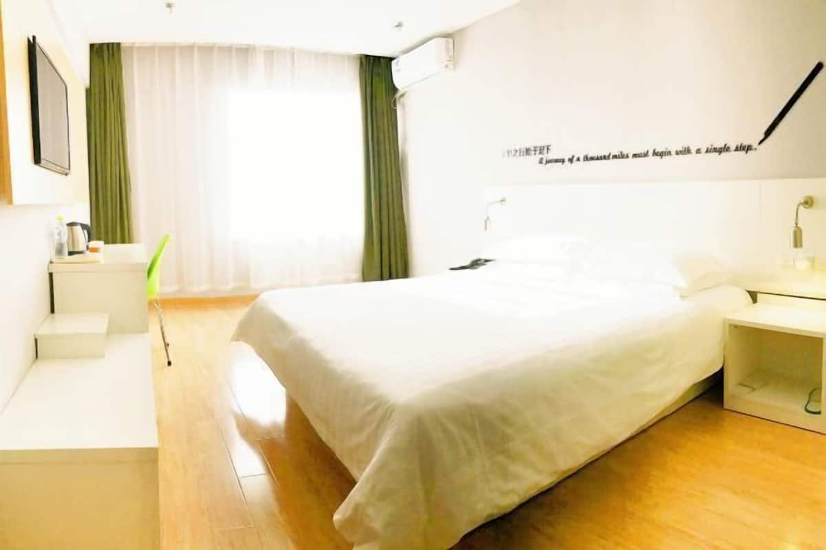 Quarto de hotel com cama, mesa de cabeceira e parede com uma citação.